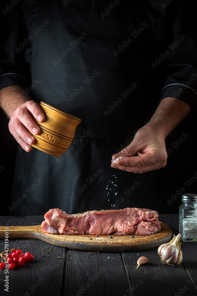 Chef prepares raw veal meat. Before baking, the chef adds salt to the ...