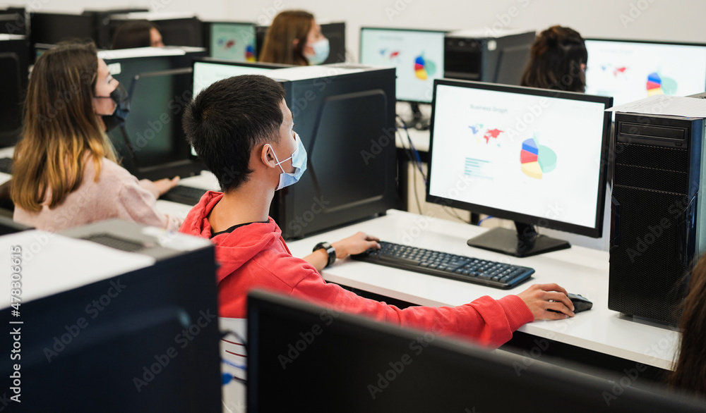 Young students using computers inside business class wearing safety ...