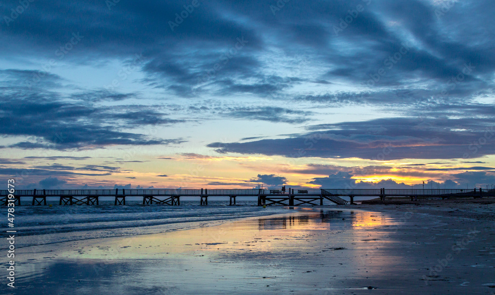 Pier going out into the sea at late sunset, partially reflected in the ...
