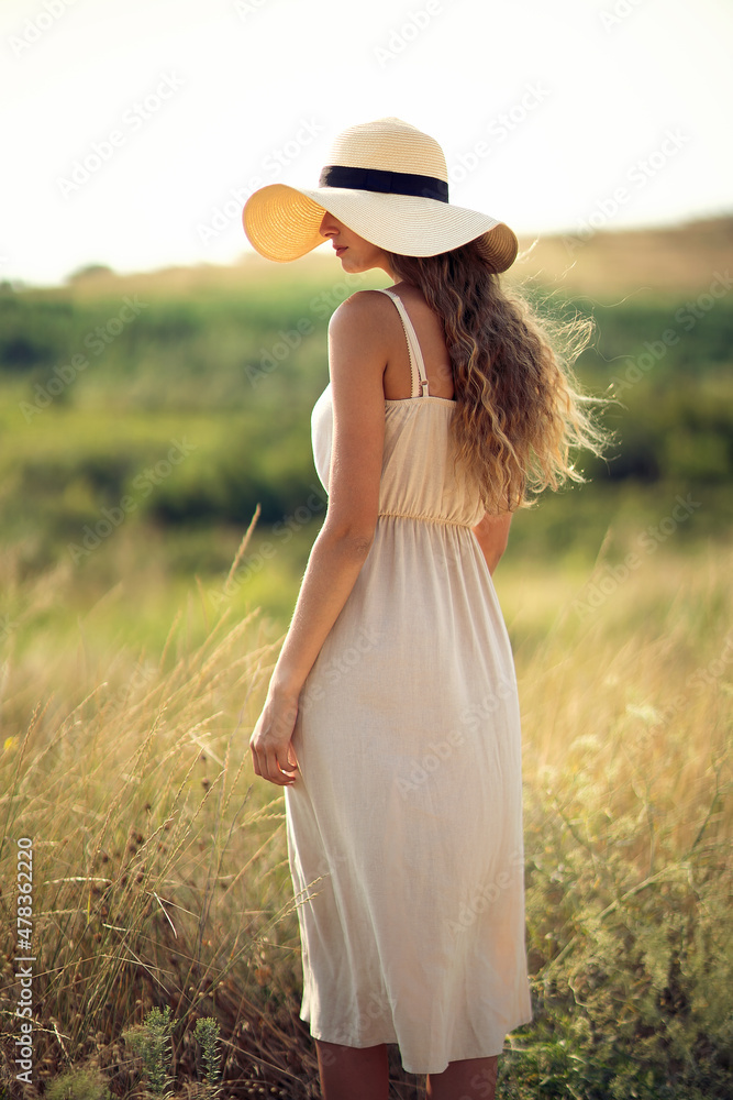Back view of beautiful girl who walks on field while wearing a sunhat ...