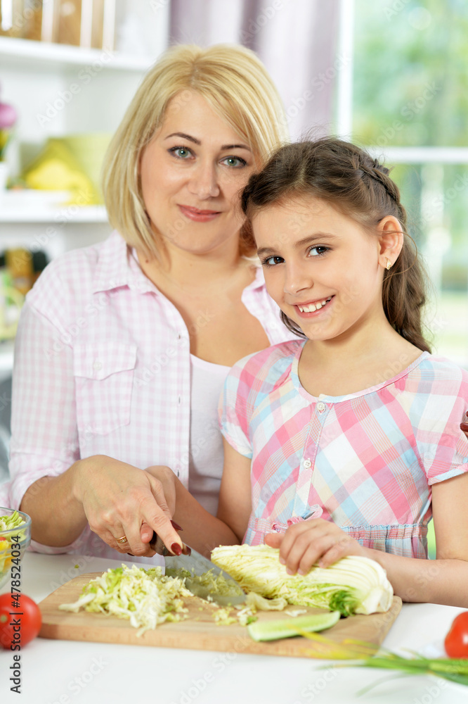 Cute little girl with her mother cooking together at kitchen table ...