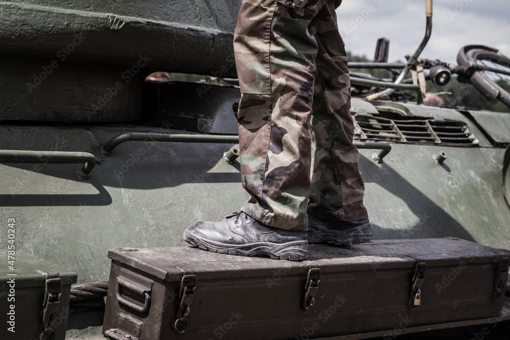 Legs of a soldier standing on metal tank, on a battlefield. Wearing ...