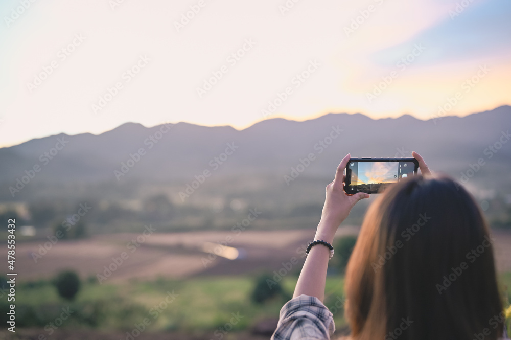 Woman use mobile phone for shoot a photograph of golden hour mountain ...