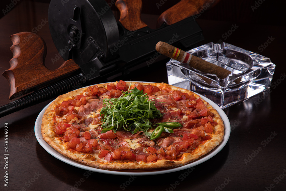 Thompson submachine gun on a dark brown table and ham pizza and a Cuban ...