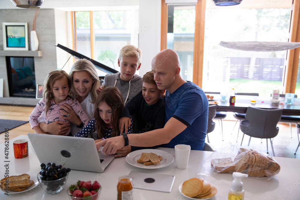 Parents using laptop in kitchen with children playing on floor Stock ...