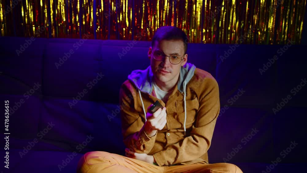 Sad man with remote control sitting on sofa and watching tv in dark ...