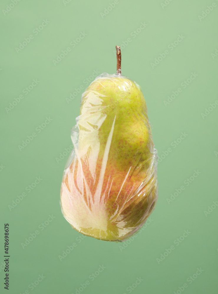 Ripe sweet pear wrapped in transparent food film. Minimalistic fruit ...