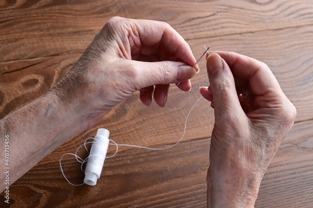 hands of an elderly woman thread a needle. Tailor's hands close-up ...