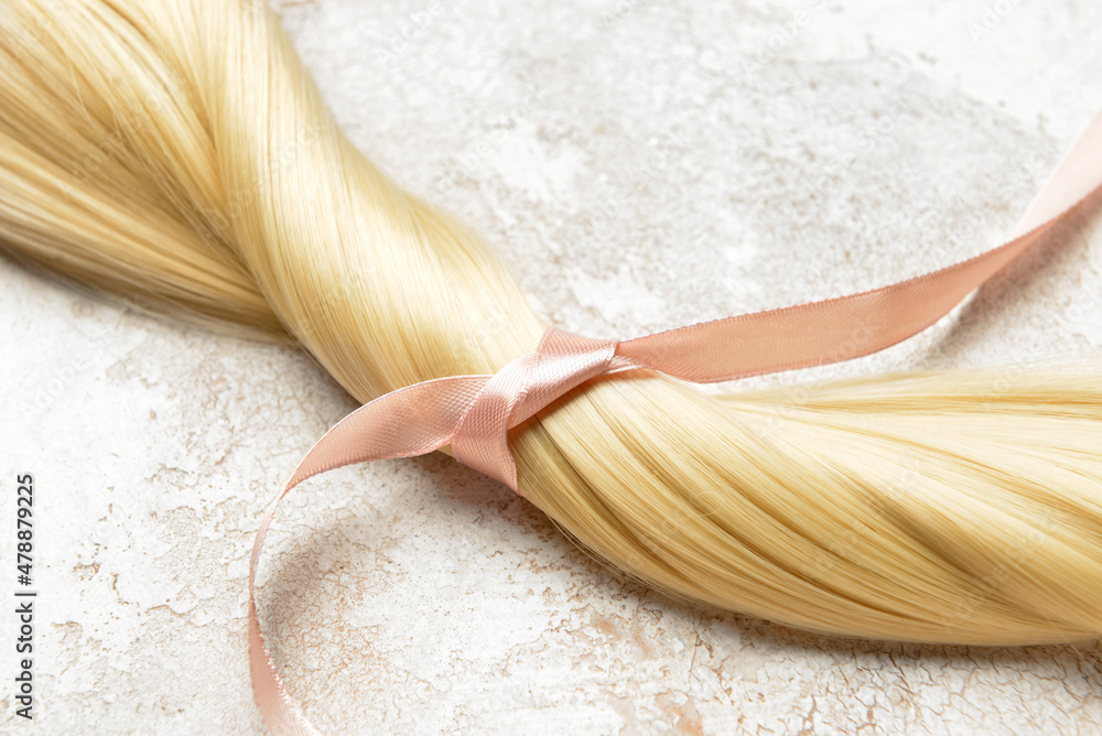 Blonde hair strand for donation with pink ribbon on grunge background ...
