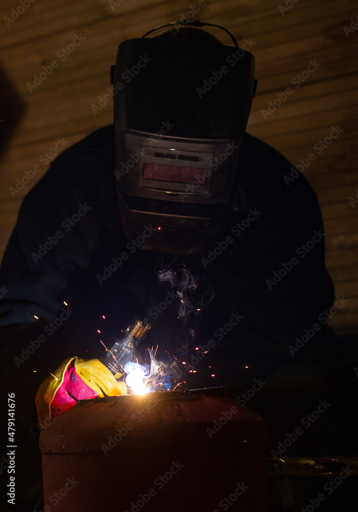 A welder in a workshop with a welding machine, welds metal structures ...