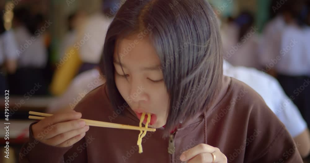 Asian female high school student eating yellow noodles with chopsticks ...