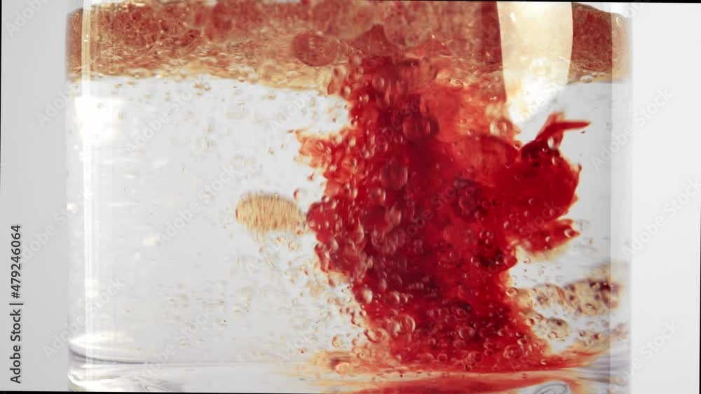 Red liquid poured into glass beaker of water, red blobs form and sink ...