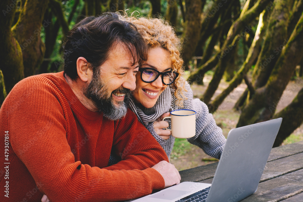 Happy modern couple use together laptop computer outdoors with trees ...