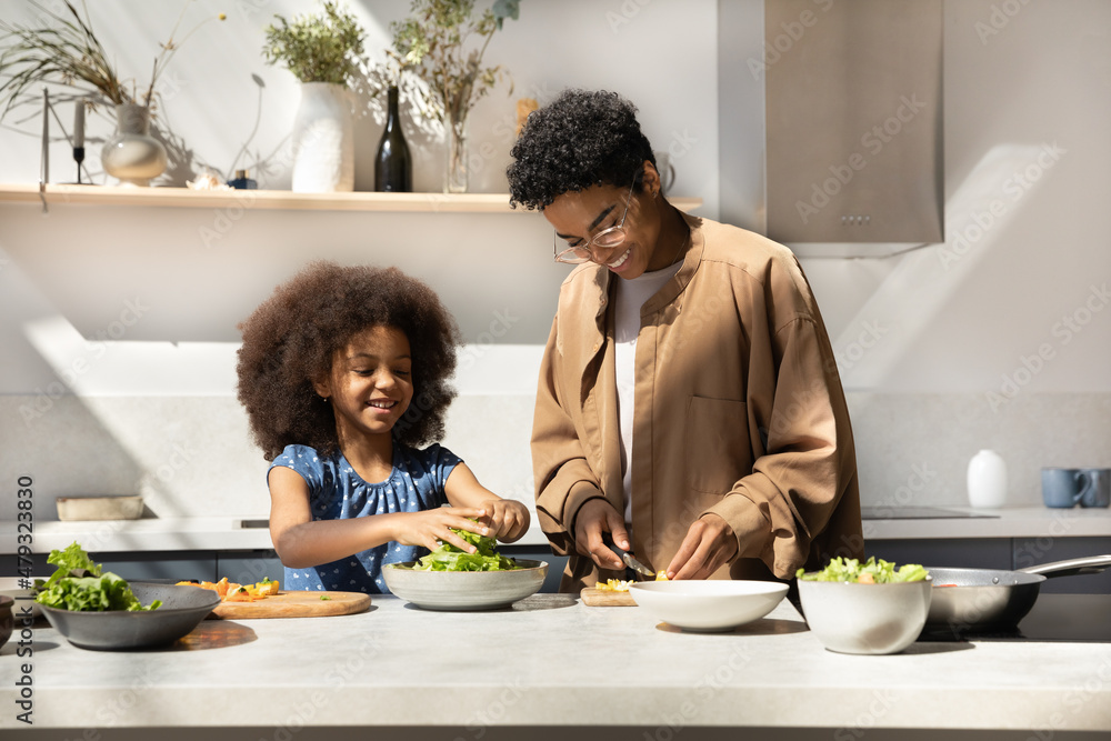 Happy African American young mom and daughter girl preparing dinner ...
