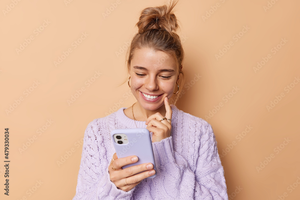 Foto de Pleased young woman smiles happily keeps index finger on cheek ...