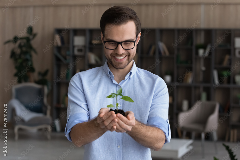 Smiling businessman wearing glasses holding small green plant sprout ...