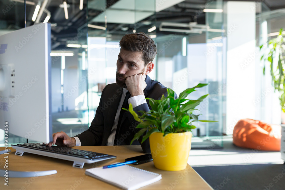 sad and thoughtful man sitting at a desk in the office at the computer ...