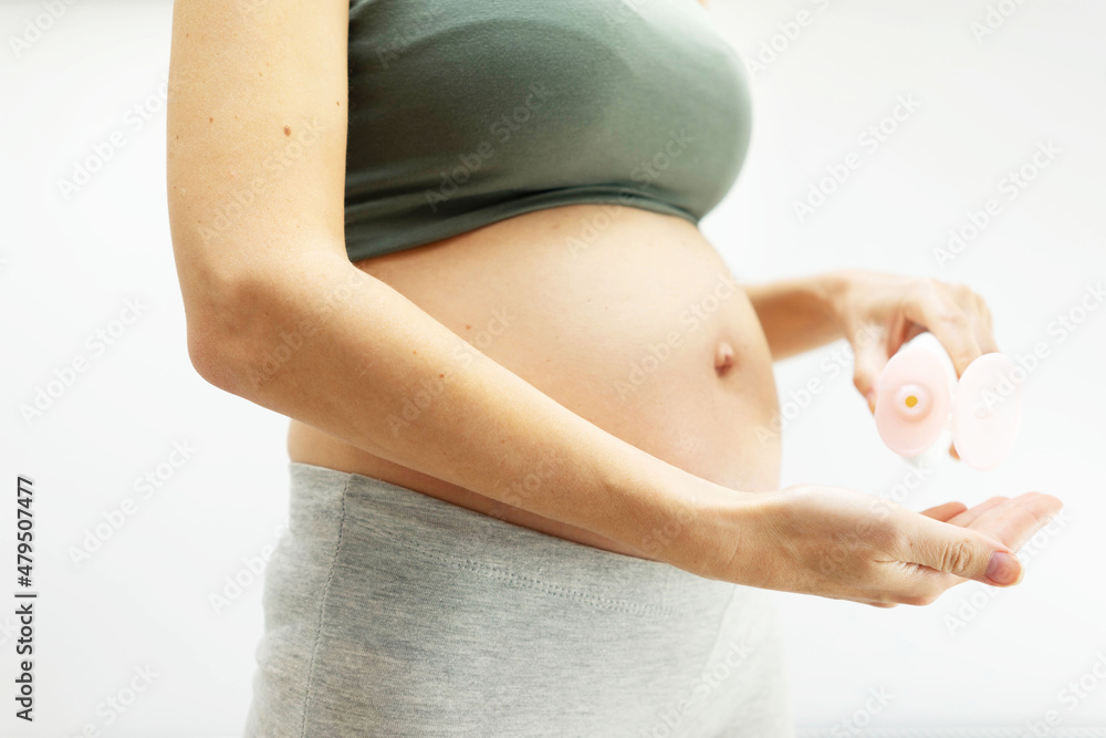 a pregnant woman smears her belly with lotion from stretch marks.The ...