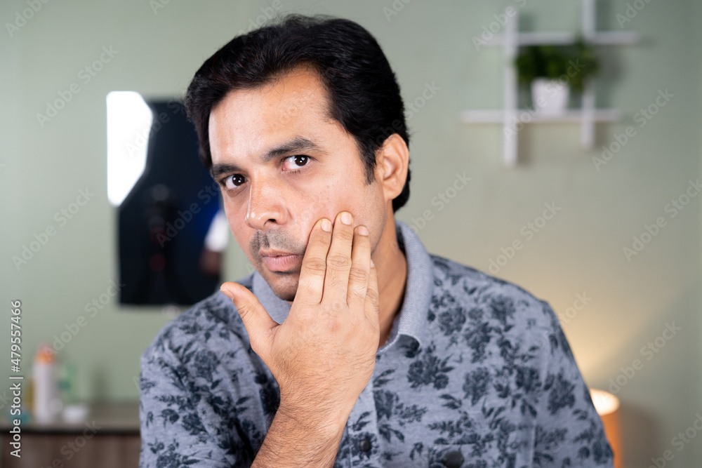 Serious handsome young man checking acne or sun tan marks on face by ...