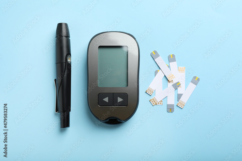 Digital glucometer, lancet pen and test strips on light blue background ...