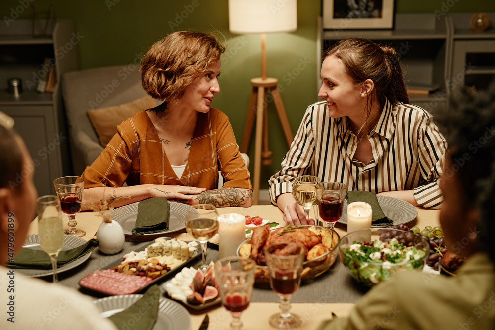 Young women talking to each other while sitting at dining table with ...