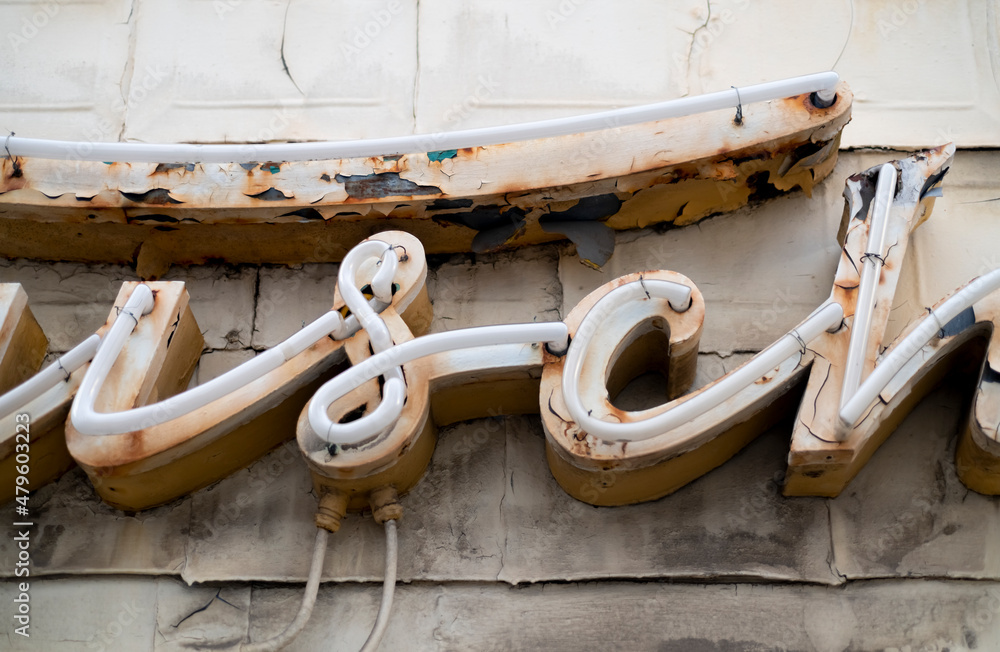 Old corroded and damaged neon letters on the beige white facade wall of ...