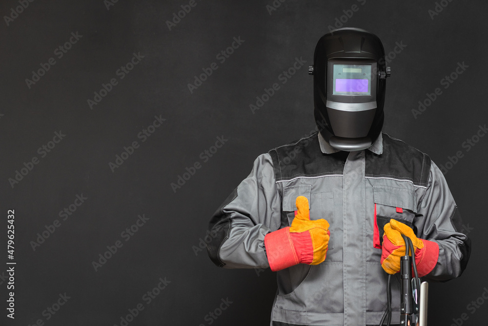 Welder man in the helmet and with welding terminals in the hand on the ...