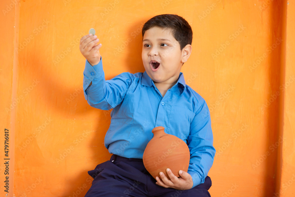 Happy cute little Indian boy holding coin in hand and clay money box or ...