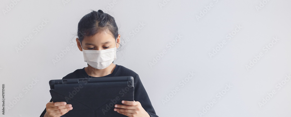 Child girl wear face mask looking tablet study online during COVID-19 ...