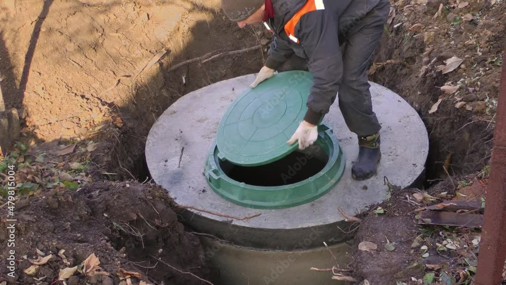 A worker installs a sewer manhole on a septic tank made of concrete ...
