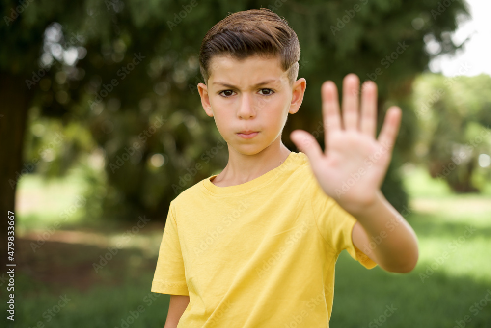 Caucasian little kid boy wearing yellow T-shirt standing outdoors shows ...