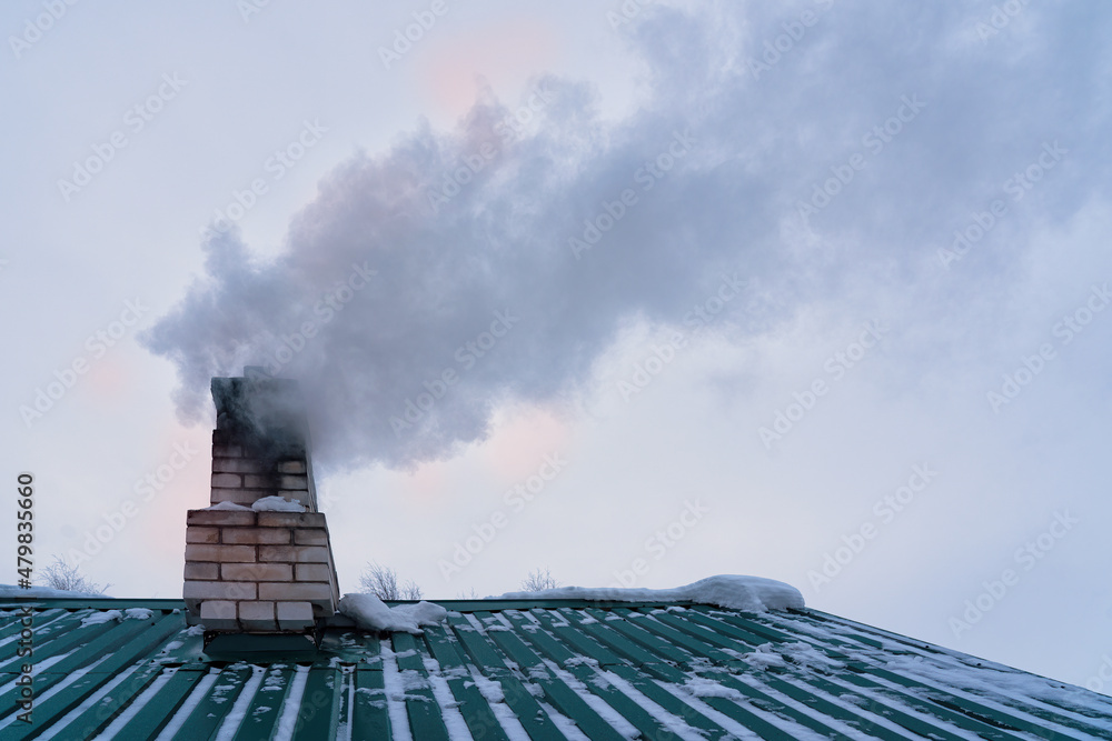 Thick smoke comes from a brick chimney on the roof of a house against a ...