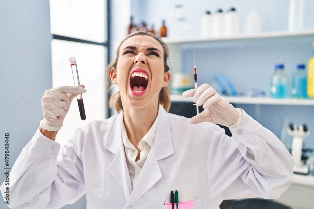 Young woman working at scientist laboratory holding blood sample angry ...