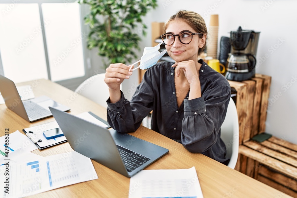 Young blonde woman working at the office wearing safety mask serious ...