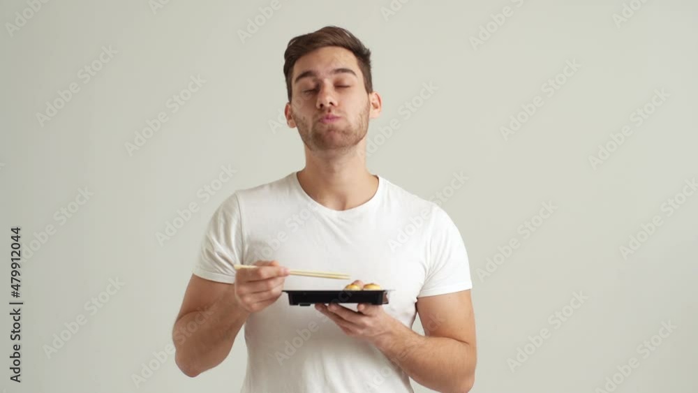 Studio portrait of handsome young man eating fresh delicious sushi ...