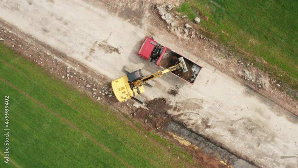 Top view of a yellow excavator loads soil from the field into a red ...