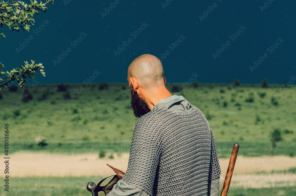 Dramatic photo of summer field before storm. A man in chain mail with a ...