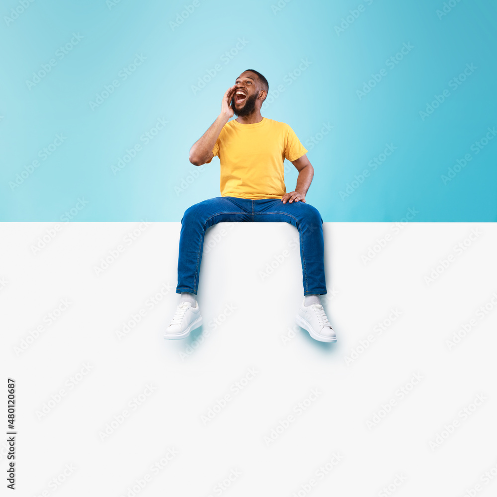 Happy black man sitting on white blank placard, shouting, announcing ...