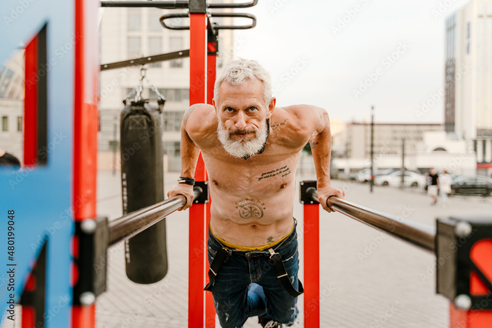Adult white shirtless man doing workout using horizontal bar outdoors ...