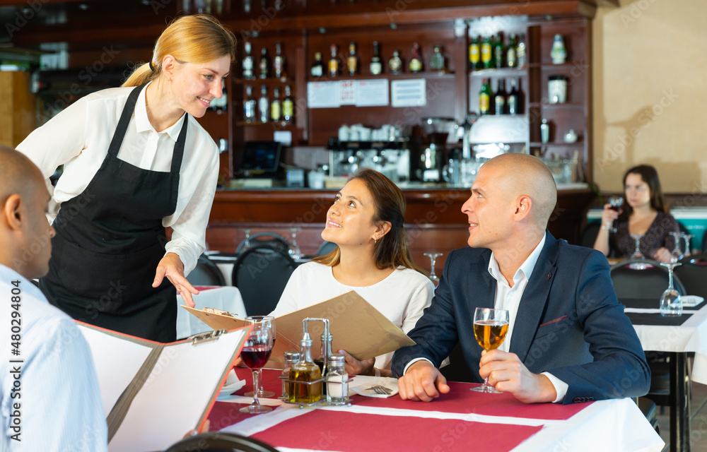 Restaurant guests will choose dish from the menu. Polite waitress helps ...