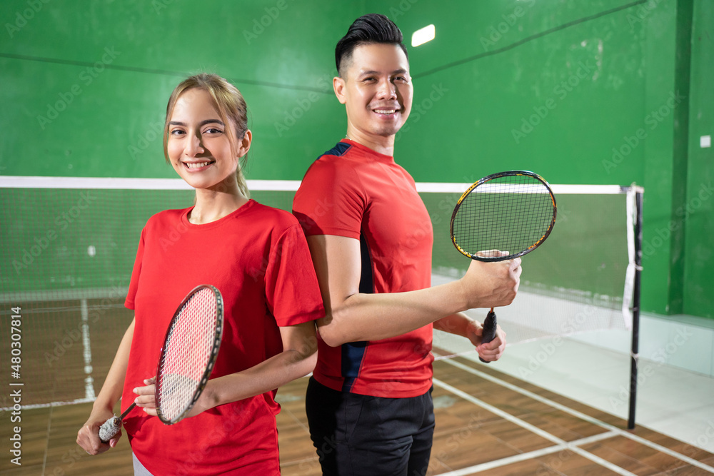 Two smiling badminton players holding rackets standing back to back ...