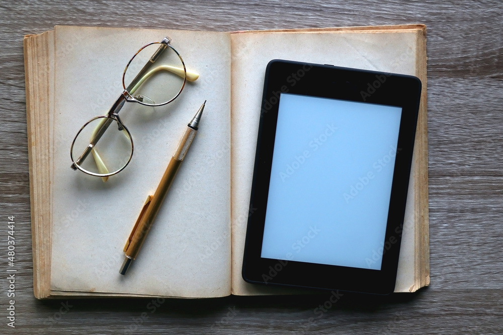 Open book, reading glasses, golden mechanical pencil and e-reader ...