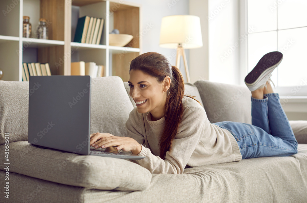 Happy woman using her laptop computer. Smiling young girl lying on a ...