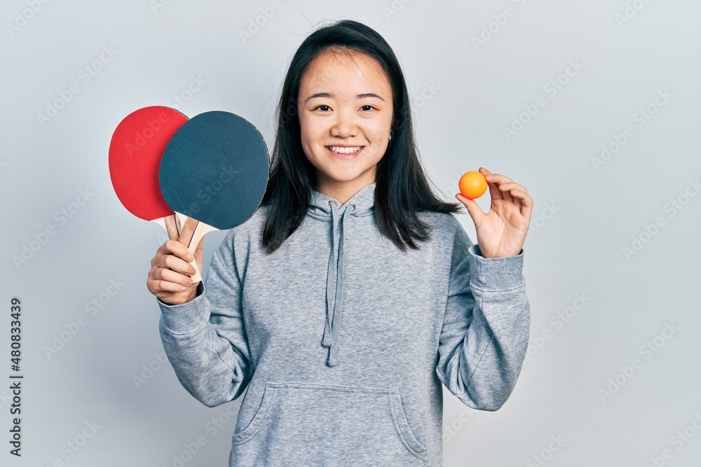 Young chinese girl holding red ping pong rackets and ball smiling with ...