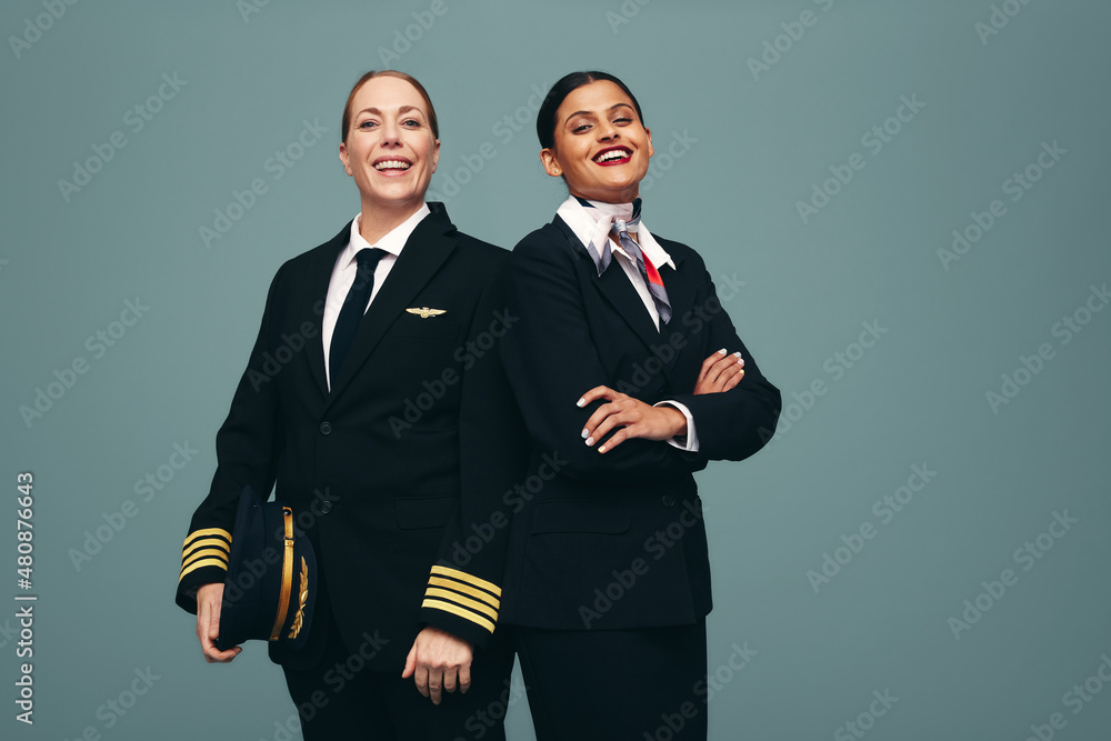 Happy pilot and flight attendant smiling at the camera in a studio ...