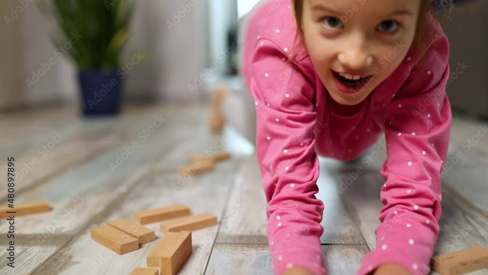 Little girl putting wooden blocks or domino in long line play blocks ...