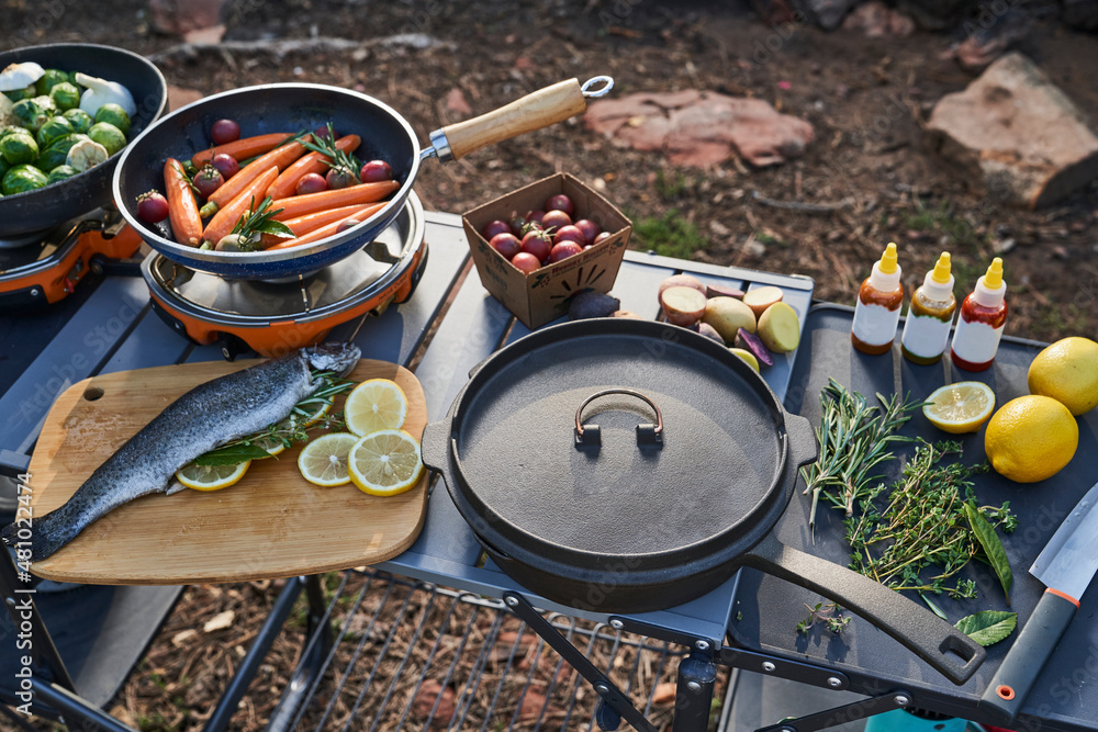 preparing camp dinner with herb stuffed trout and vegetables. Stock ...