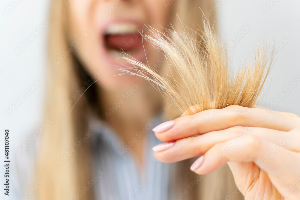 A shocked and upset blond woman holds the damaged brittle dry split ...