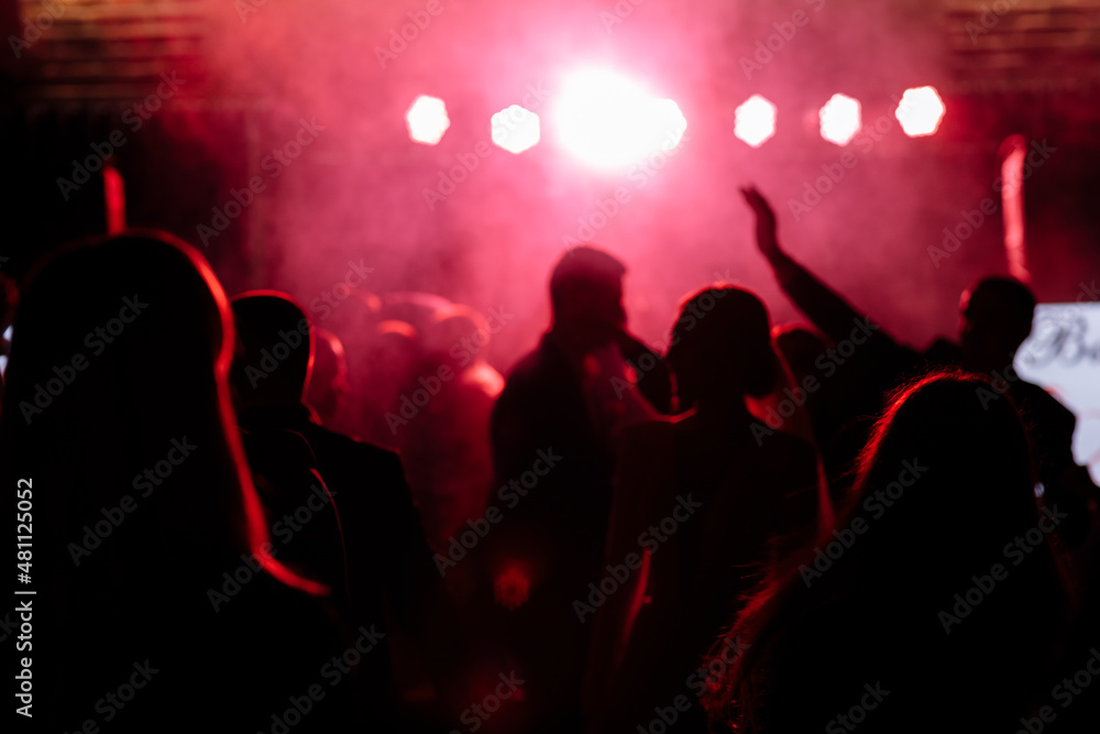 cheering crowd in front of bright red stage lights. Silhouette image of ...