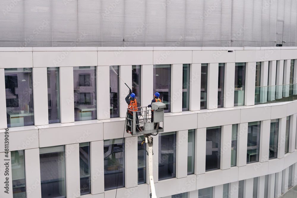 Two workers wearing safety harness wash office building facade at ...